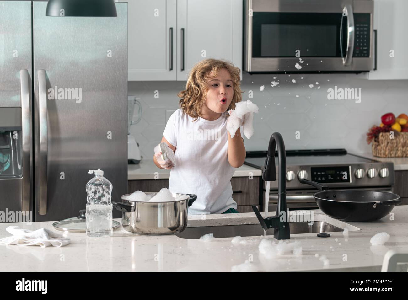 Child washing dishes near sink in kitchen. Child with sponge with dish ...