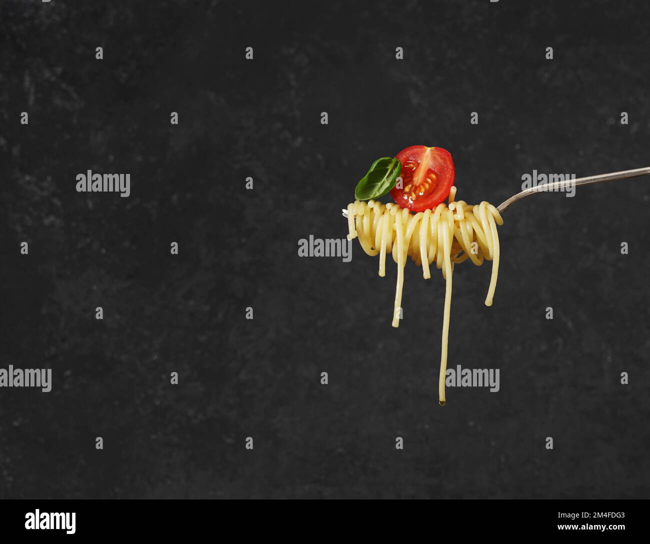 Yellow long spaghetti on a fork with basi leaf ant tomato on dark ...