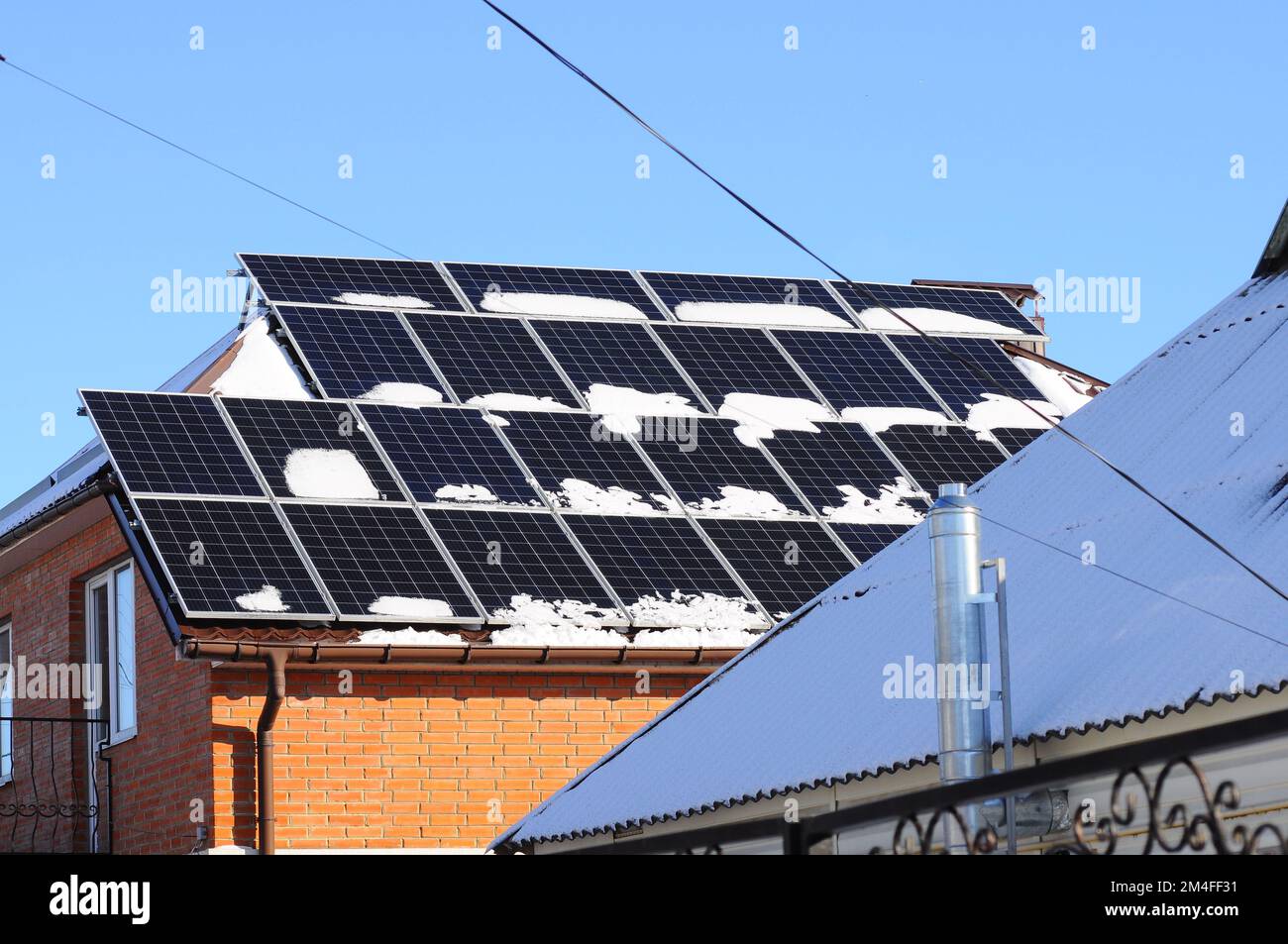 Snow-covered solar panels are mounted on the roof of a private house ...