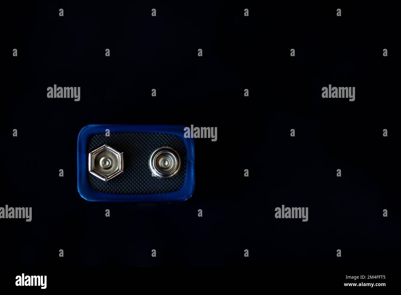 A closeup top view of a 9v type battery with blue edges on a black ...