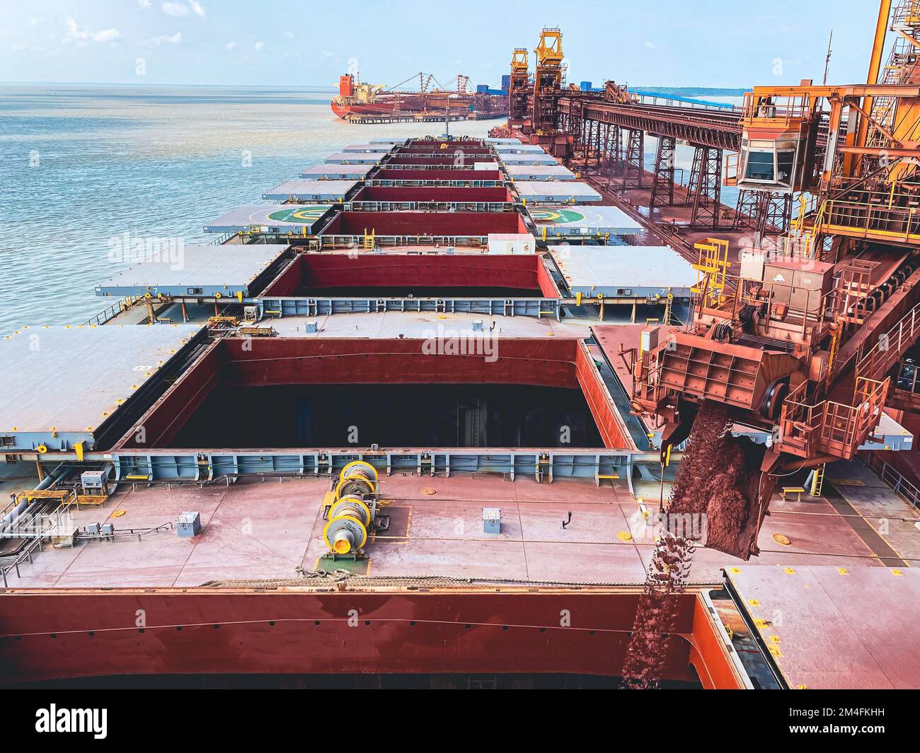 An iron ore conveyor loading cargo in the bulk carrier with a cloudy ...