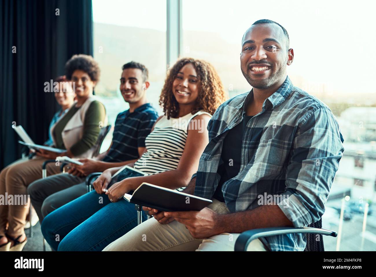 Portrait of a group of young cheerful work colleagues seated on chairs ...