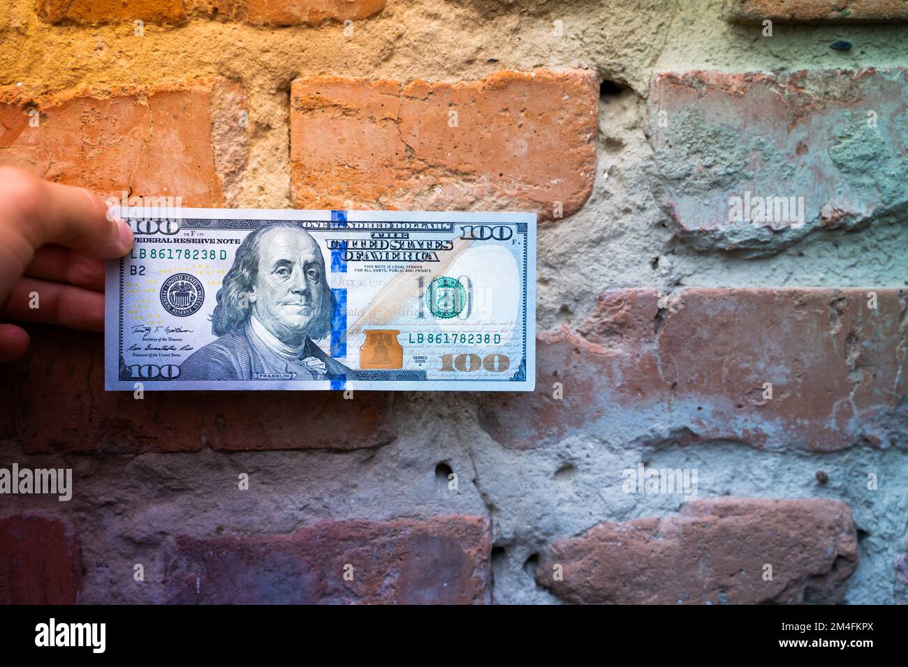A hand holds a hundred dollar bill against the background of an old ...