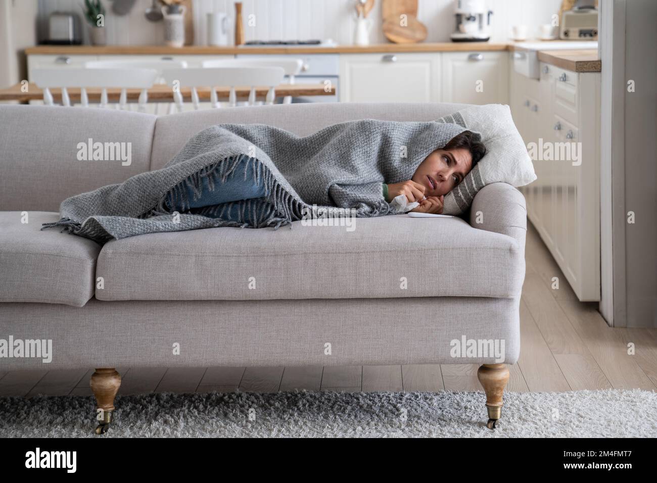 Sick female covered with wool blanket plaid resting on couch, feeling ...
