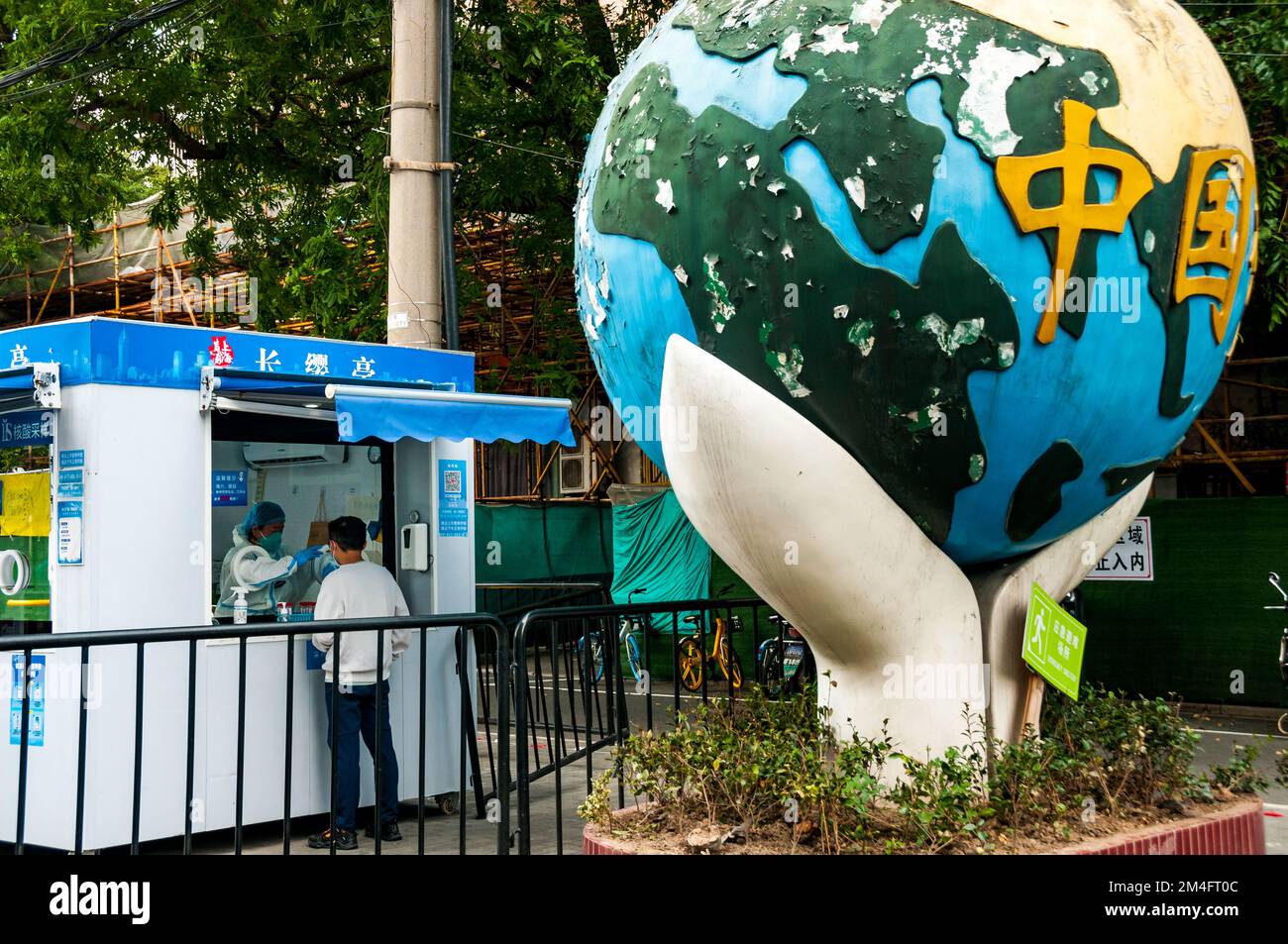 A faded China Dream globe with a PCR testing station behind in Dongmen ...