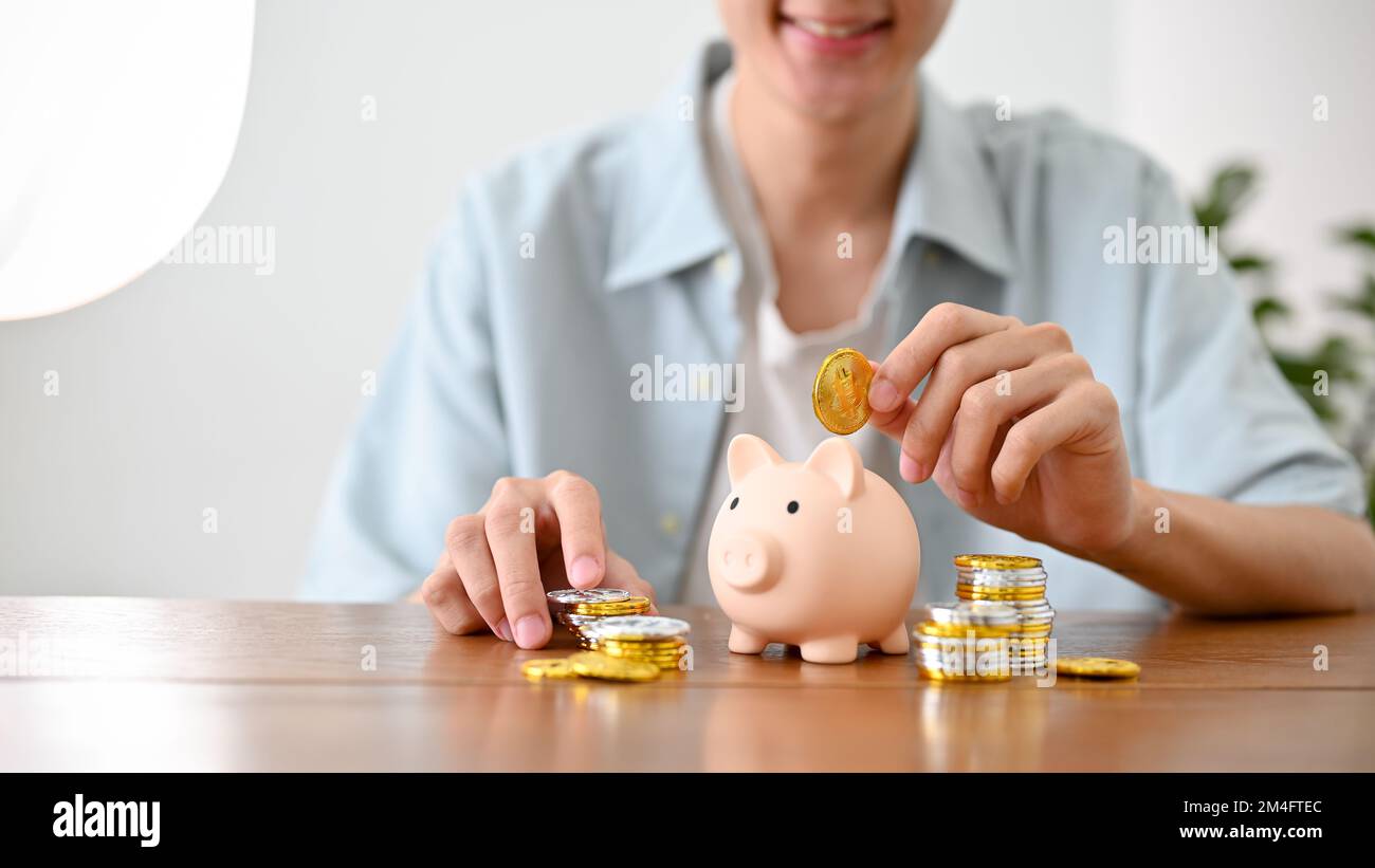 Happy young Asian man inserts coins into a piggy bank, saving money for ...