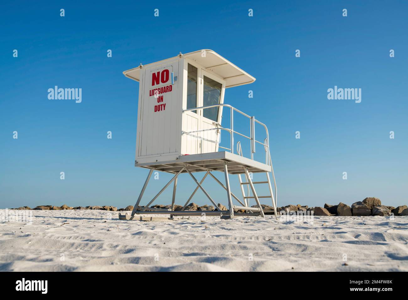 Front side view of a white lifeguard tower against the rocks and blue ...