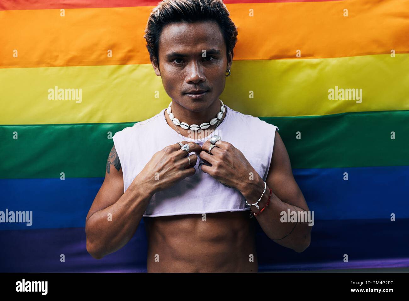 Portrait of a young stylish guy against LGBT rainbow flag looking at ...