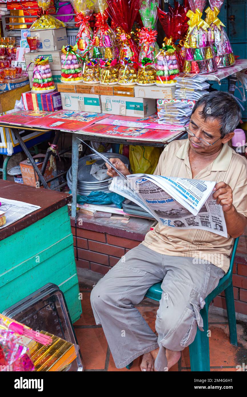 Vietnamese trader reading newspaper in souvenir shop at Duc Thanh Tran ...