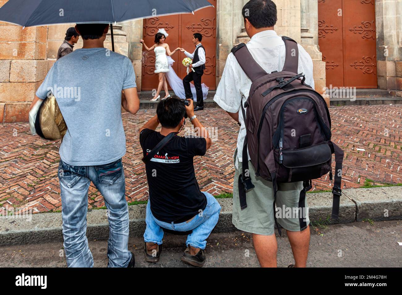 Vietnamese professional photographer setting up contemporary wedding photo with team and young ...