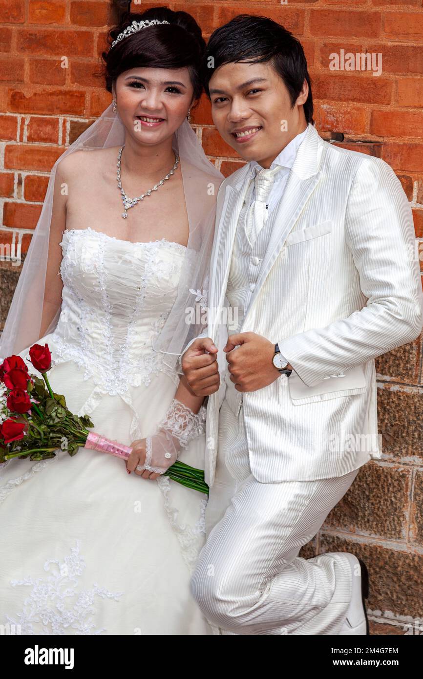 Young Vietnamese couple in white posing with bouquet for wedding photo ...