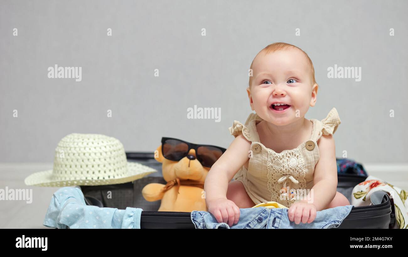 Happy baby girl sitting in travel suitcase with clothes smiles and ...