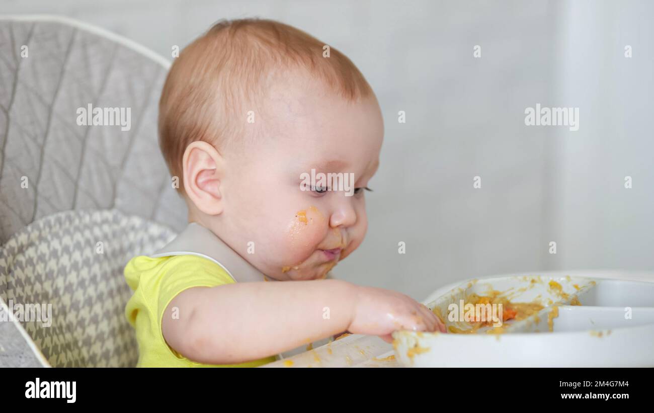 Excited baby girl touches food leftovers on plate and tries to taste ...
