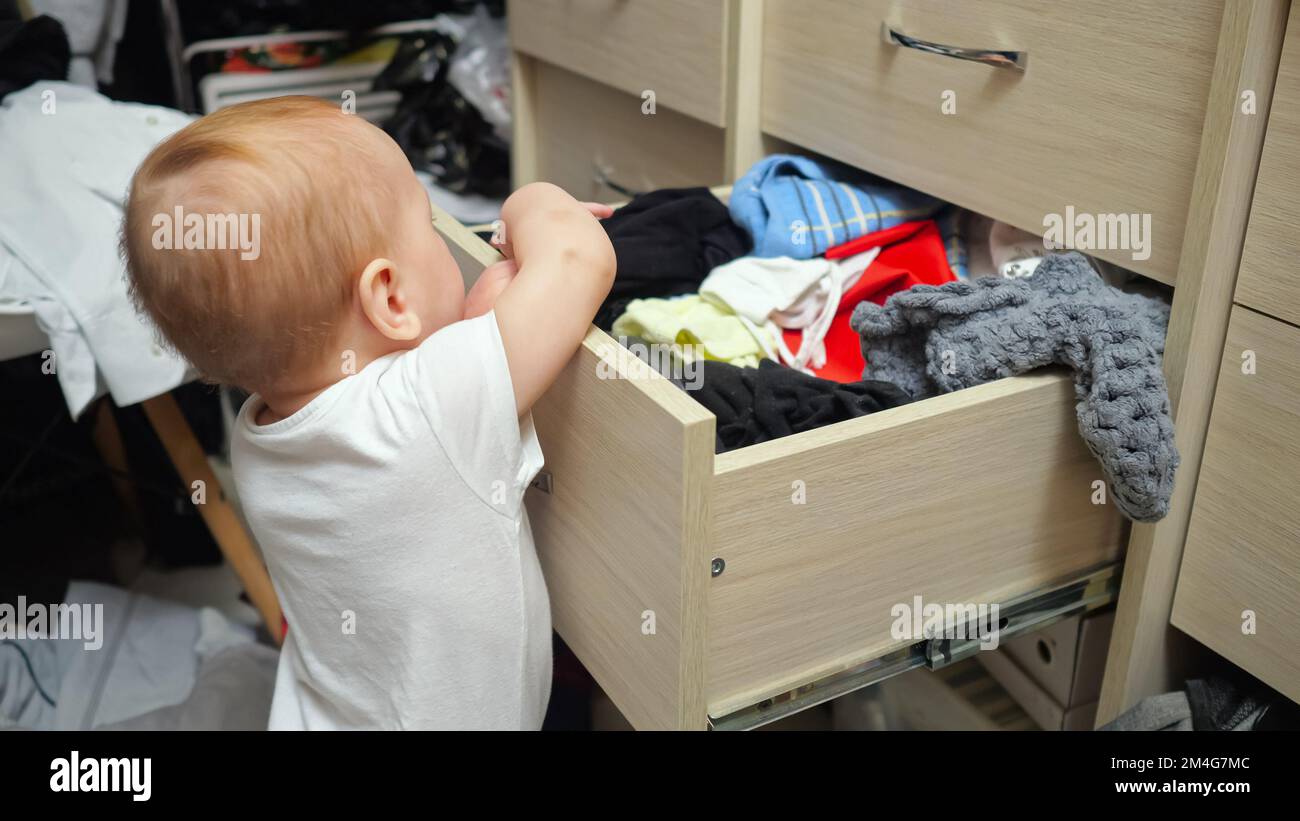 Baby girl with excited and amused expression opens cabinet drawer and ...