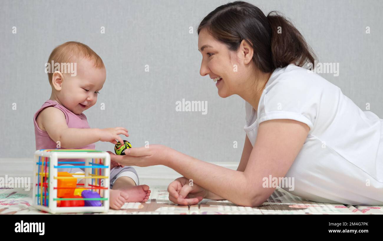 Mother plays with baby daughter against white wall. Child with excited ...