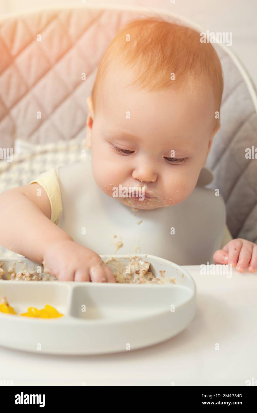 Excited baby girl touches food leftovers on plate and tries to taste ...