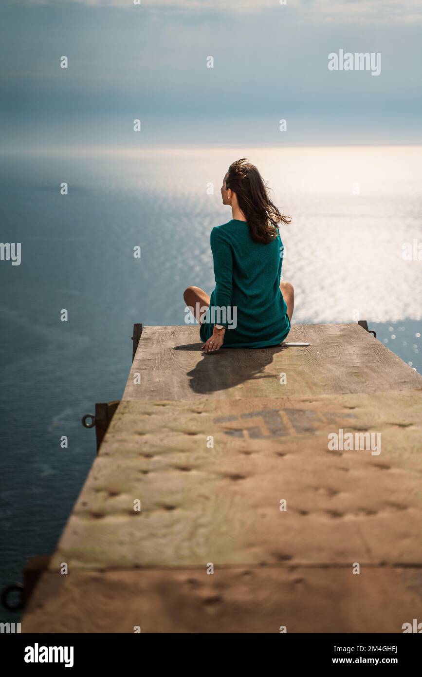 A girl sits on a wooden springboard for jumping with a rope. In a dark ...
