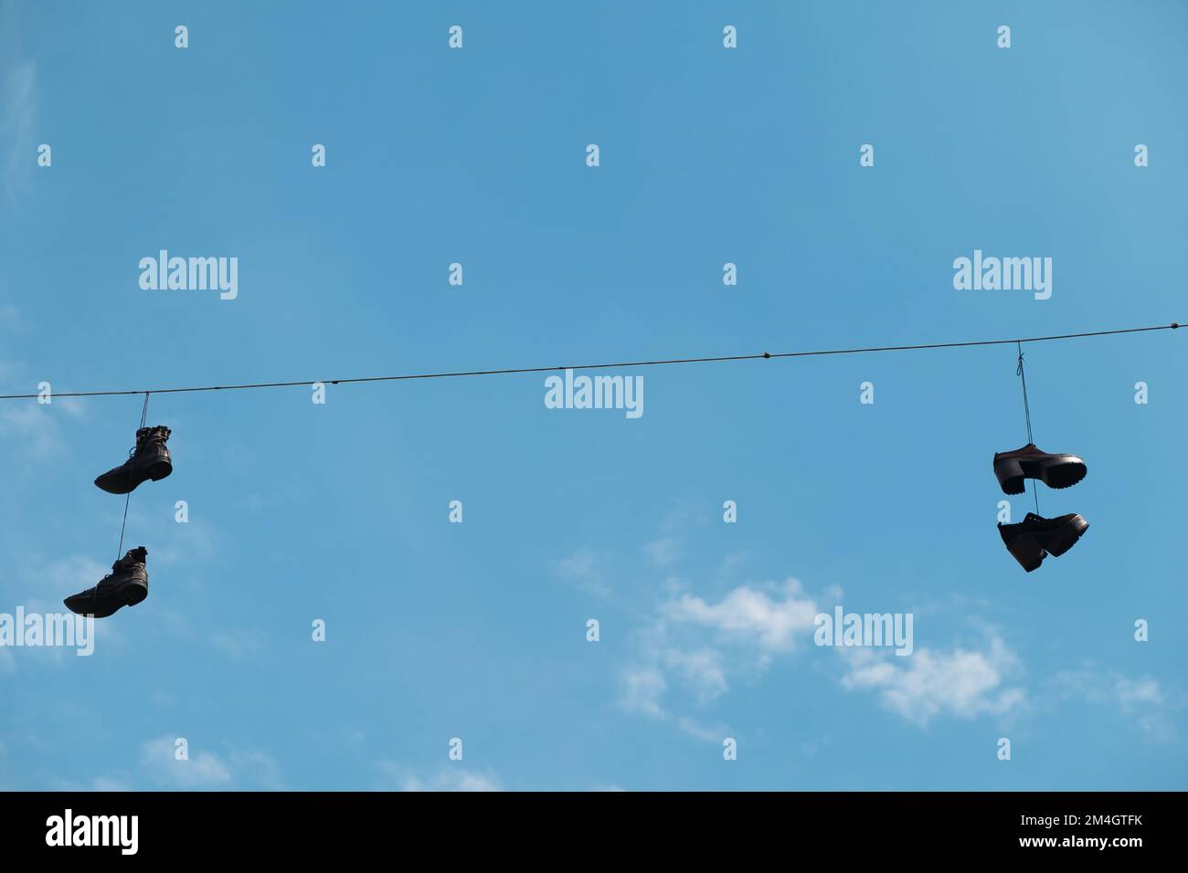 Two pairs of shoes tied at the laces hangs on both ends of a wire ...