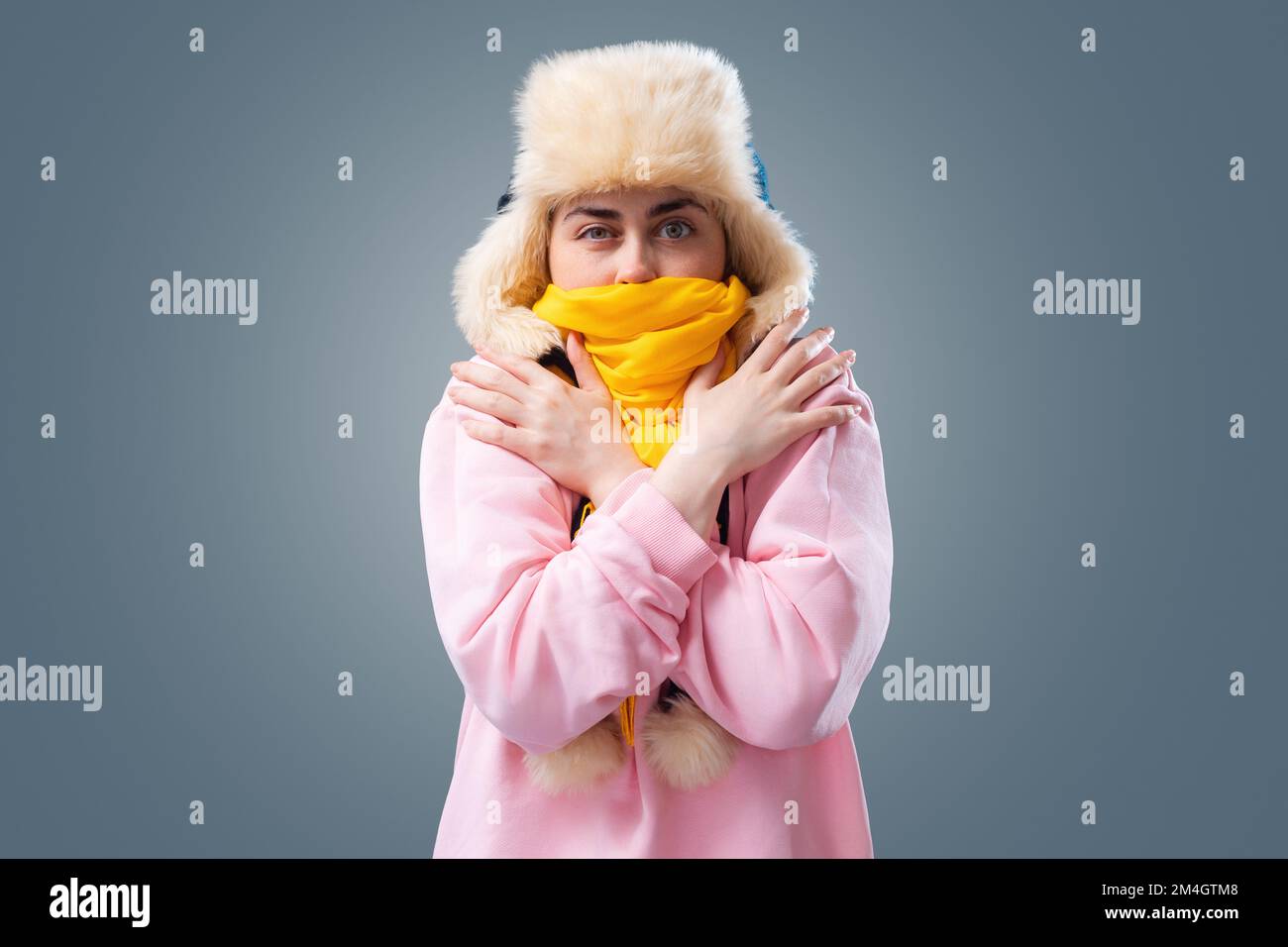 Freezed young woman in a ushanka hat and scarf is breathing, hugging ...
