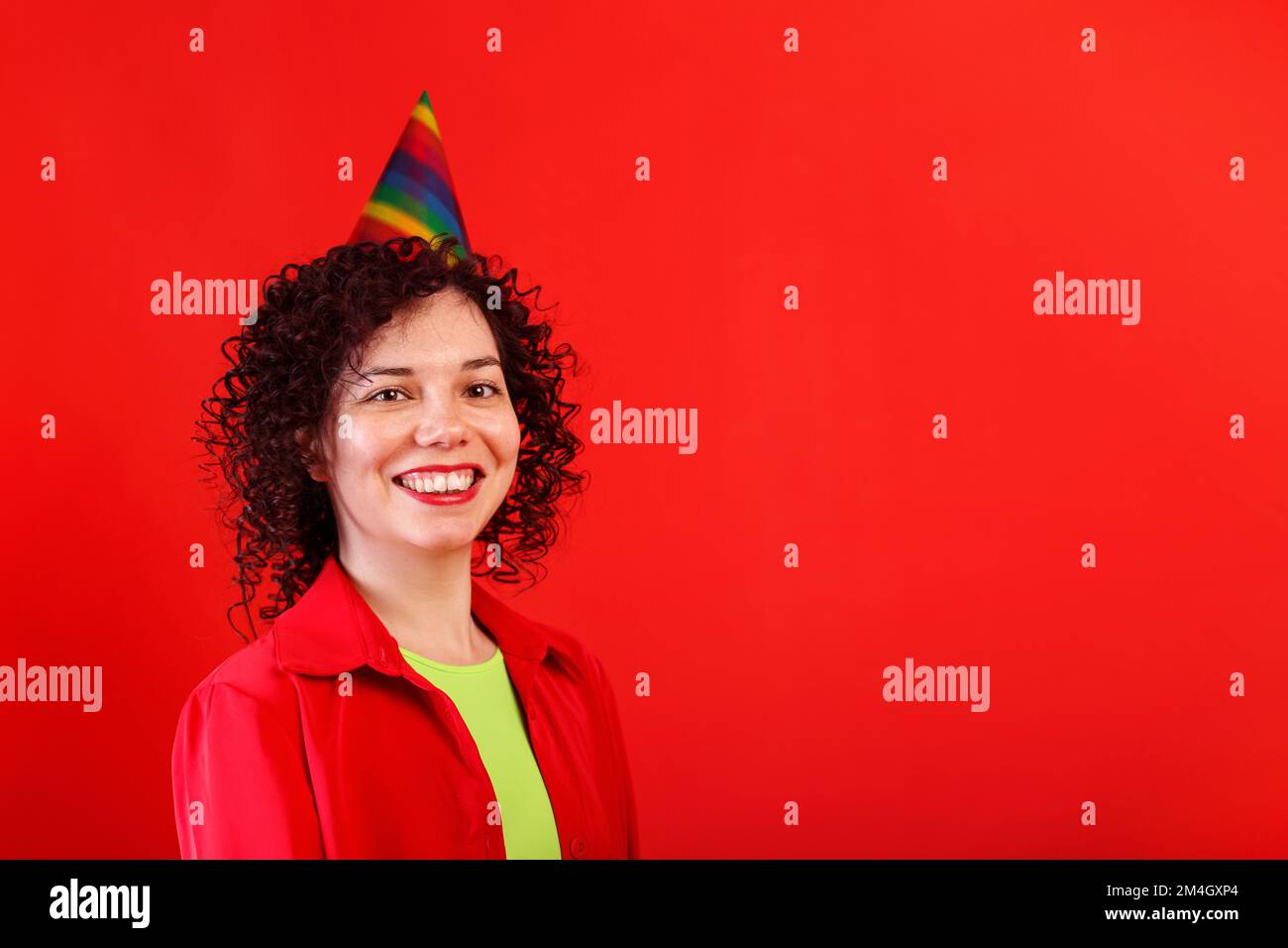 Shy Curly Haired Girl In Bright Red Shirt And Colorful Party Hat