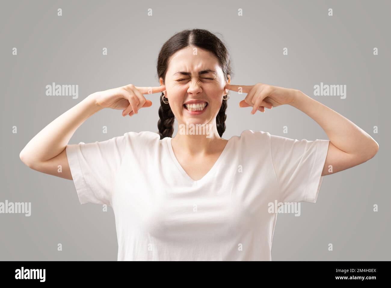 Portrait of a young suffering woman painfully clutching her ears with ...