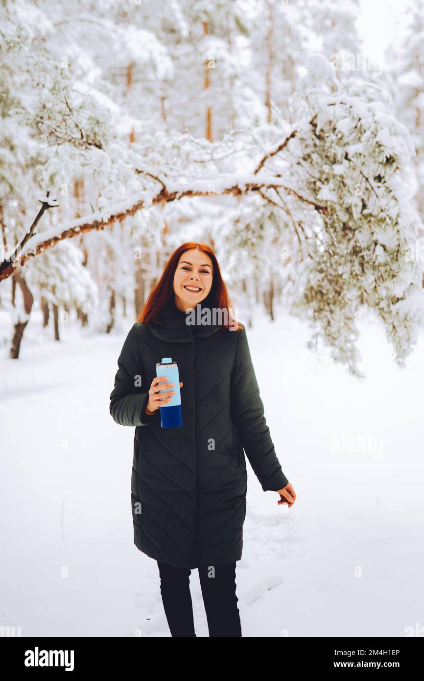 Cheerful girl with red hair in warm clothes playing with snow outdoors ...
