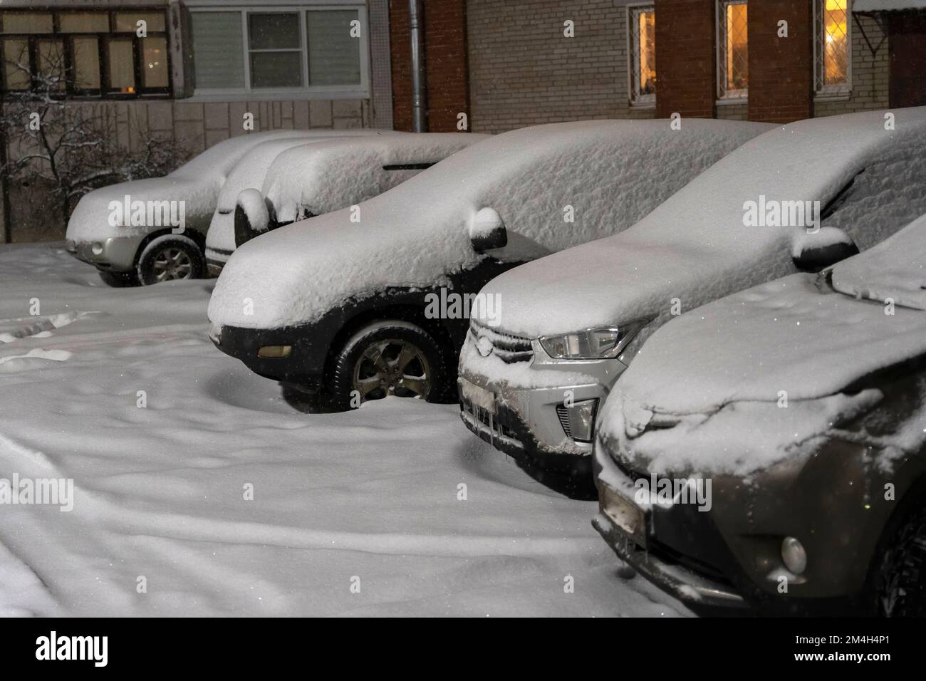 Snow-covered cars parked in a row in an open parking lot in the yard ...
