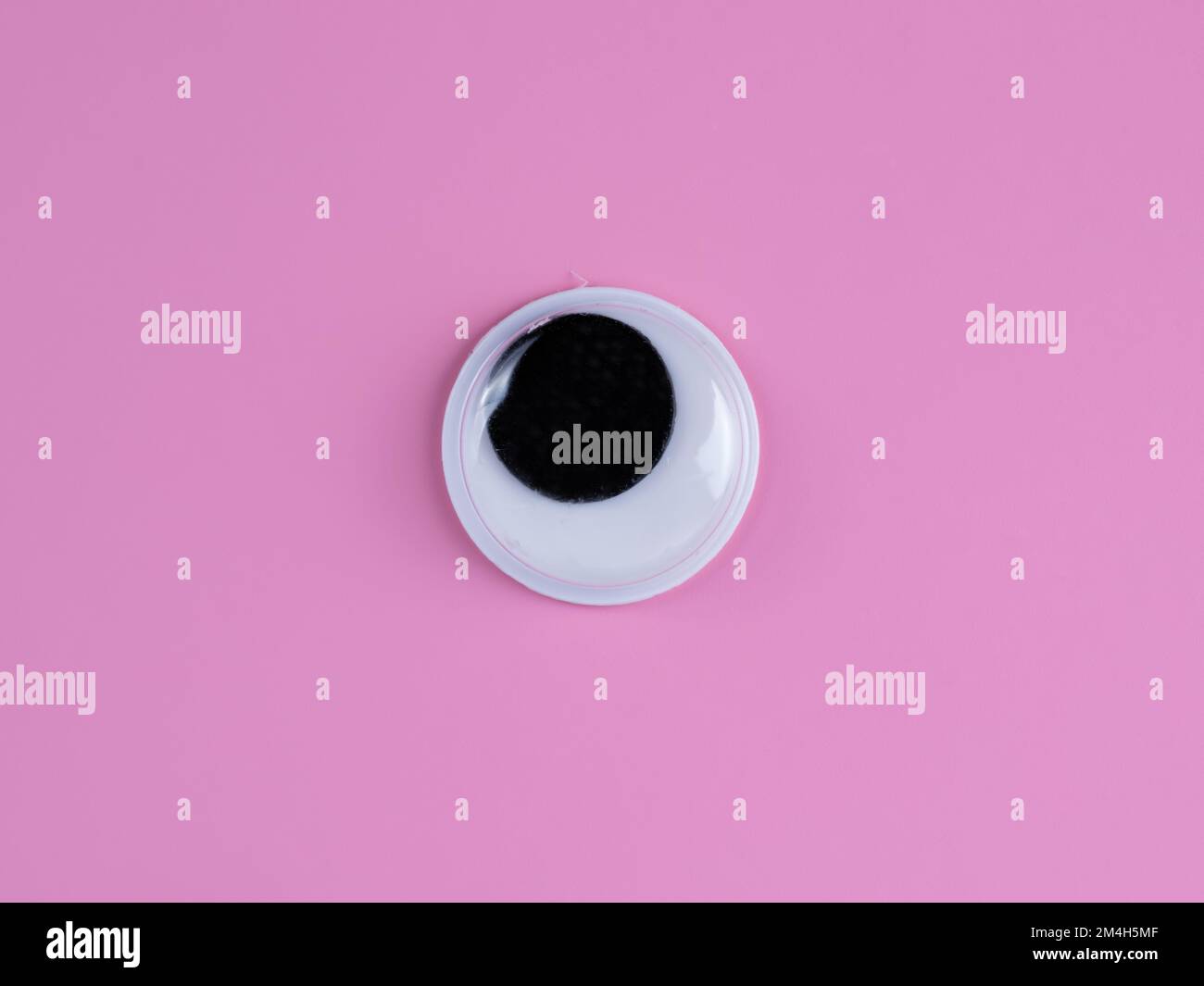 single wobbly googly eye isolated on a pink background with copyspace ...