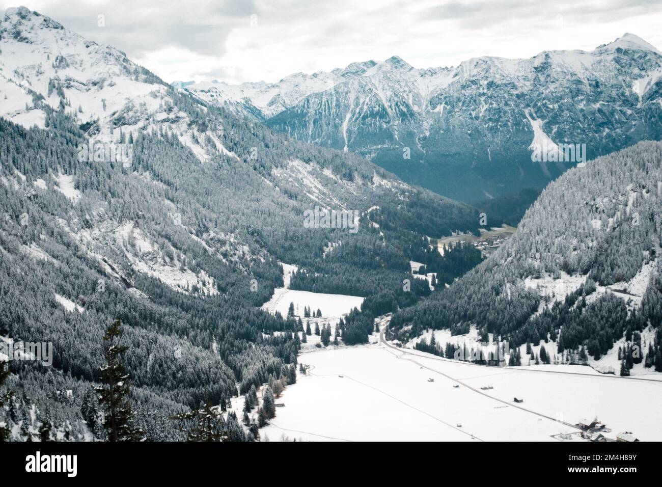 An aerial view of snowy valley surrounded by mountain forests in winter ...