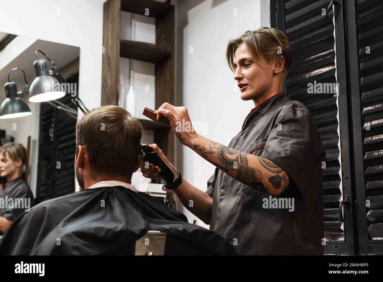 Woman barber cutting and styling hair of man in barber shop Stock Photo ...