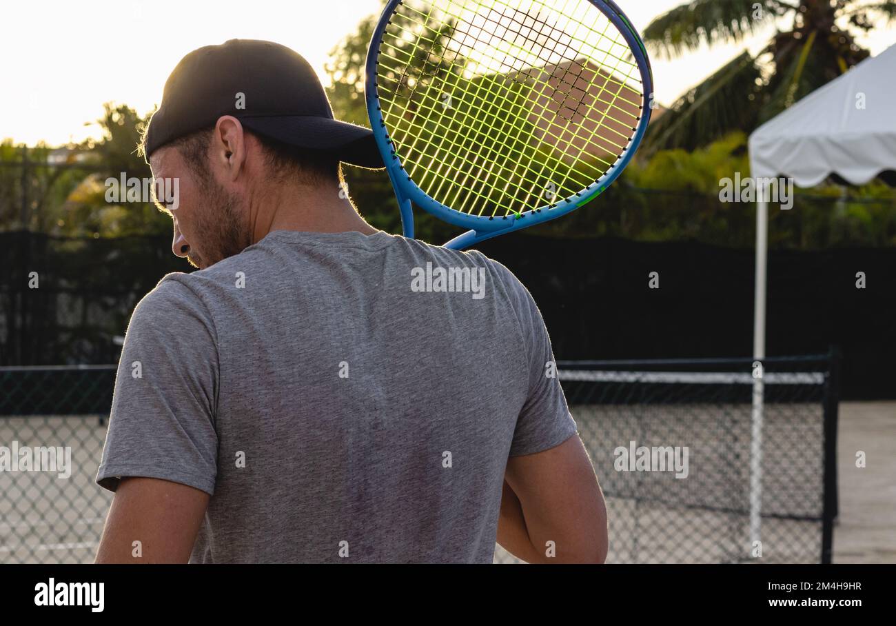 Rear view of male tennis player outdoors, a man wearing cap holds ...