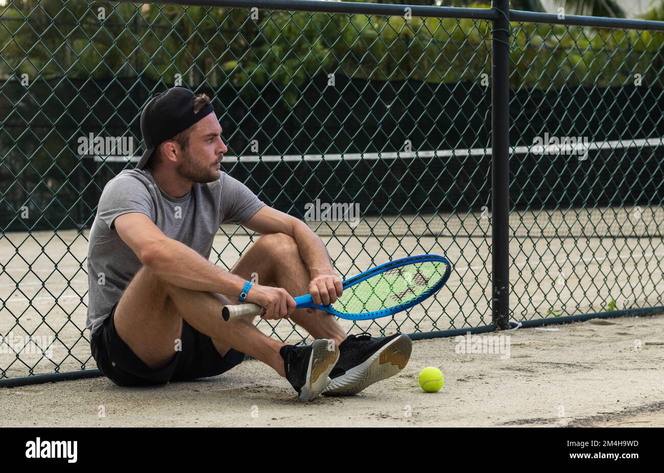 Man tennis player in cap sitting on the tennis court and resting after ...