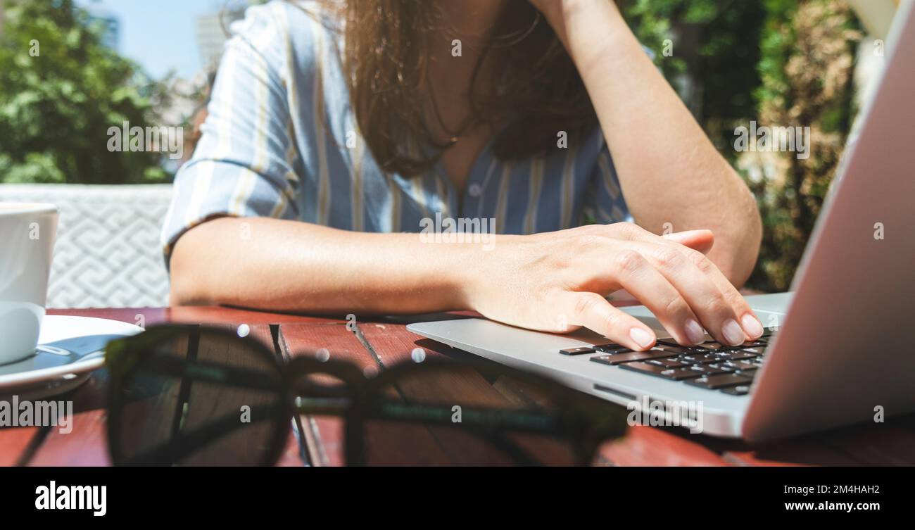 Female person using her laptop while sitting outdoor cafe in summer ...