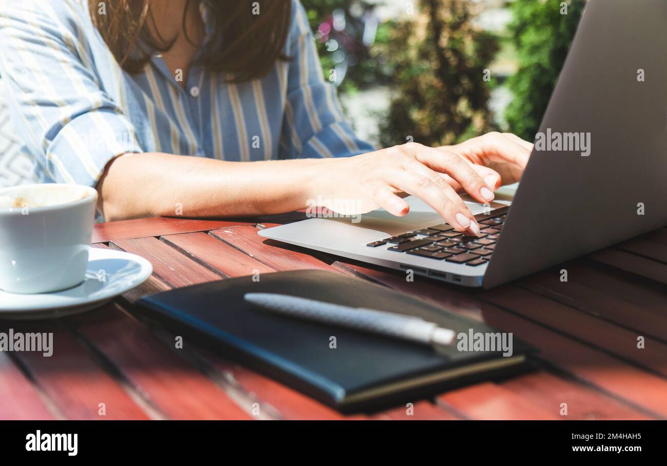 Female person using her laptop while sitting outdoor cafe in summer ...
