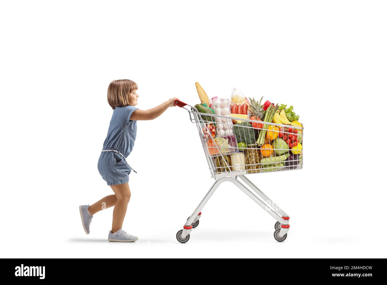 Full length profile shot of a little girl pushing a big shopping cart isolated on white ...