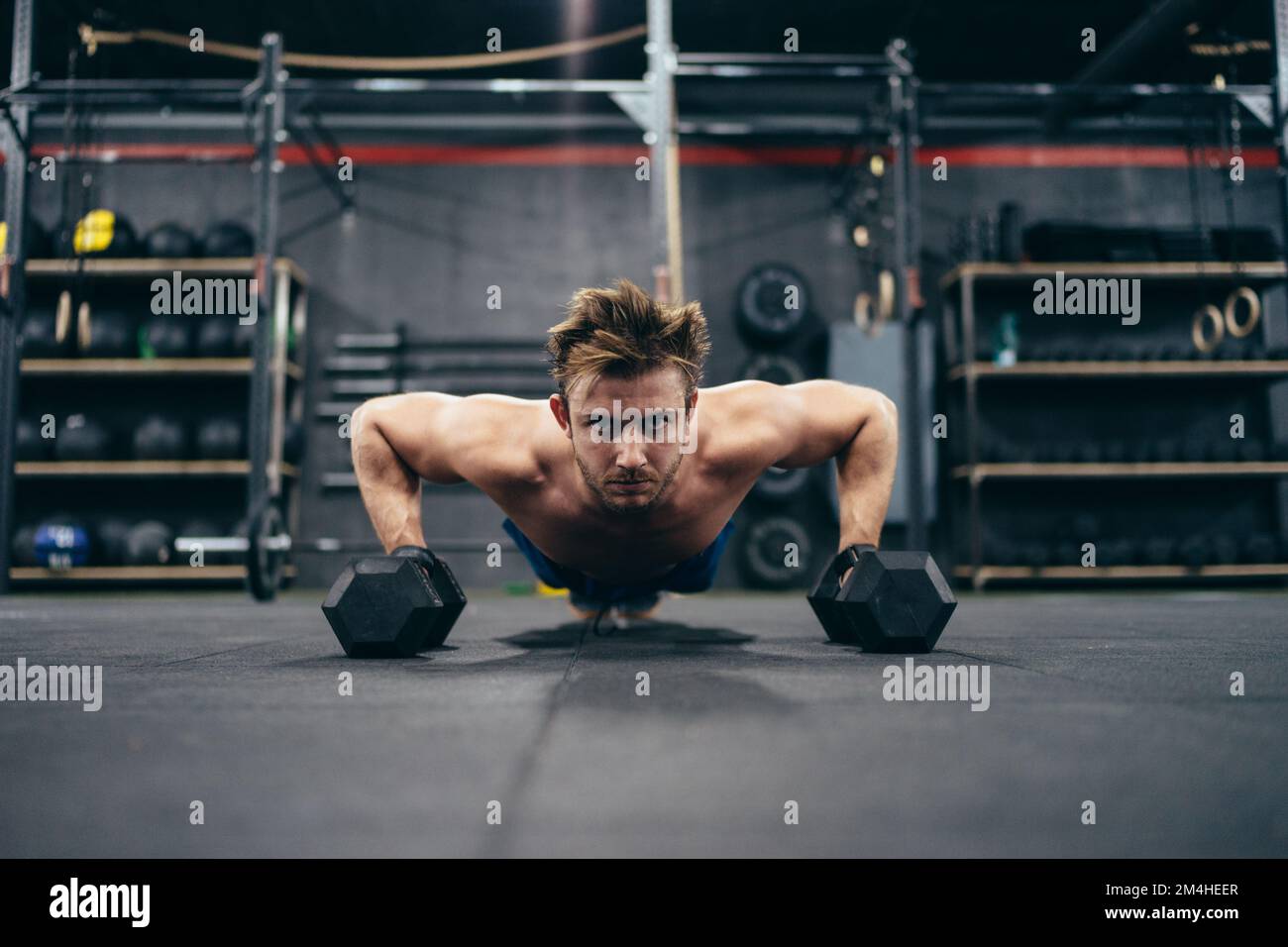 Portrait of a strong man doing push-ups using dumbbells in a gym Stock ...