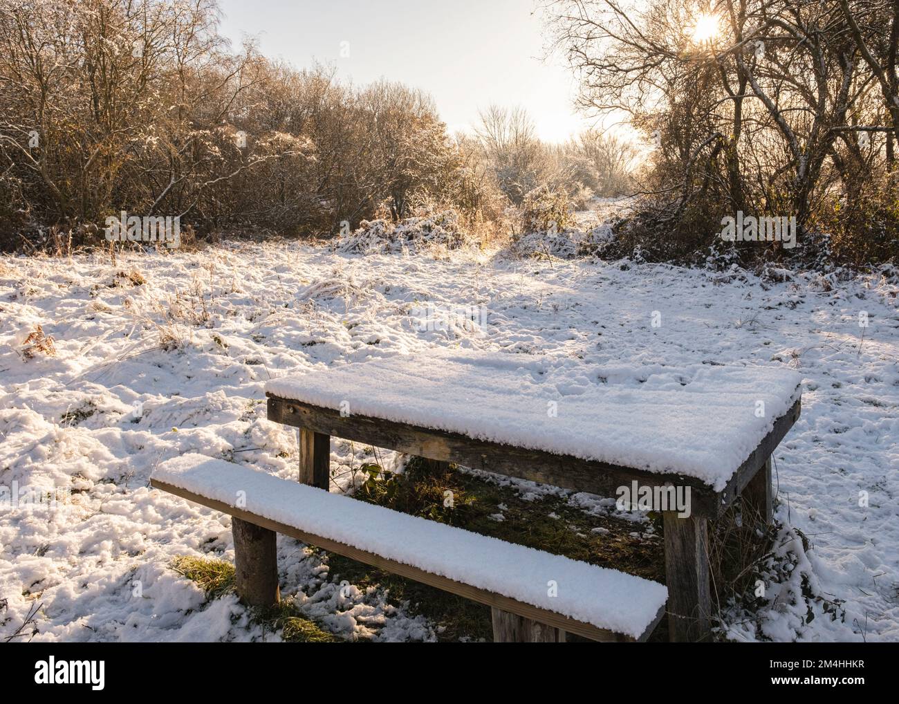 A snow covered cold lonely picnic table in winter with sun shining ...