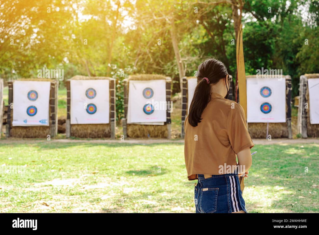 Back view of Asian girl wear face mask aims archery bow and arrow to ...