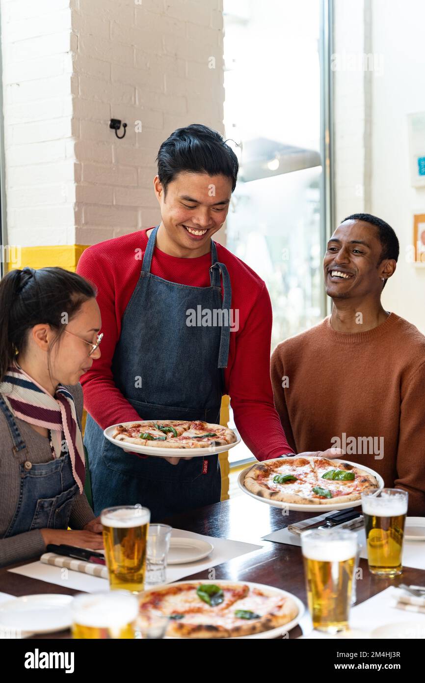 Waiter serving delicious pizza to a group of friends sitting in a ...
