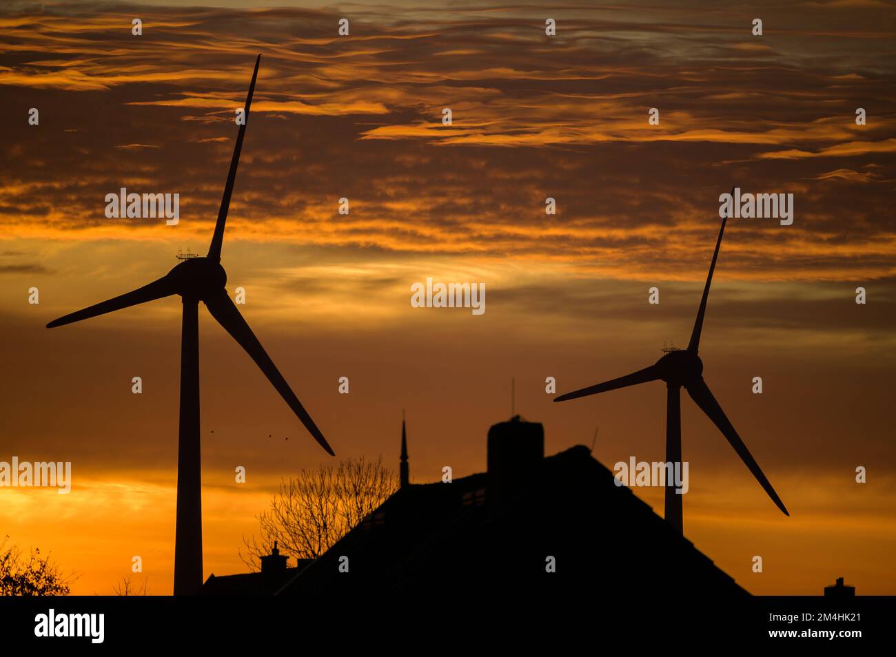 Two wind turbines against spectacular sunrise sky with clouds and roof ...
