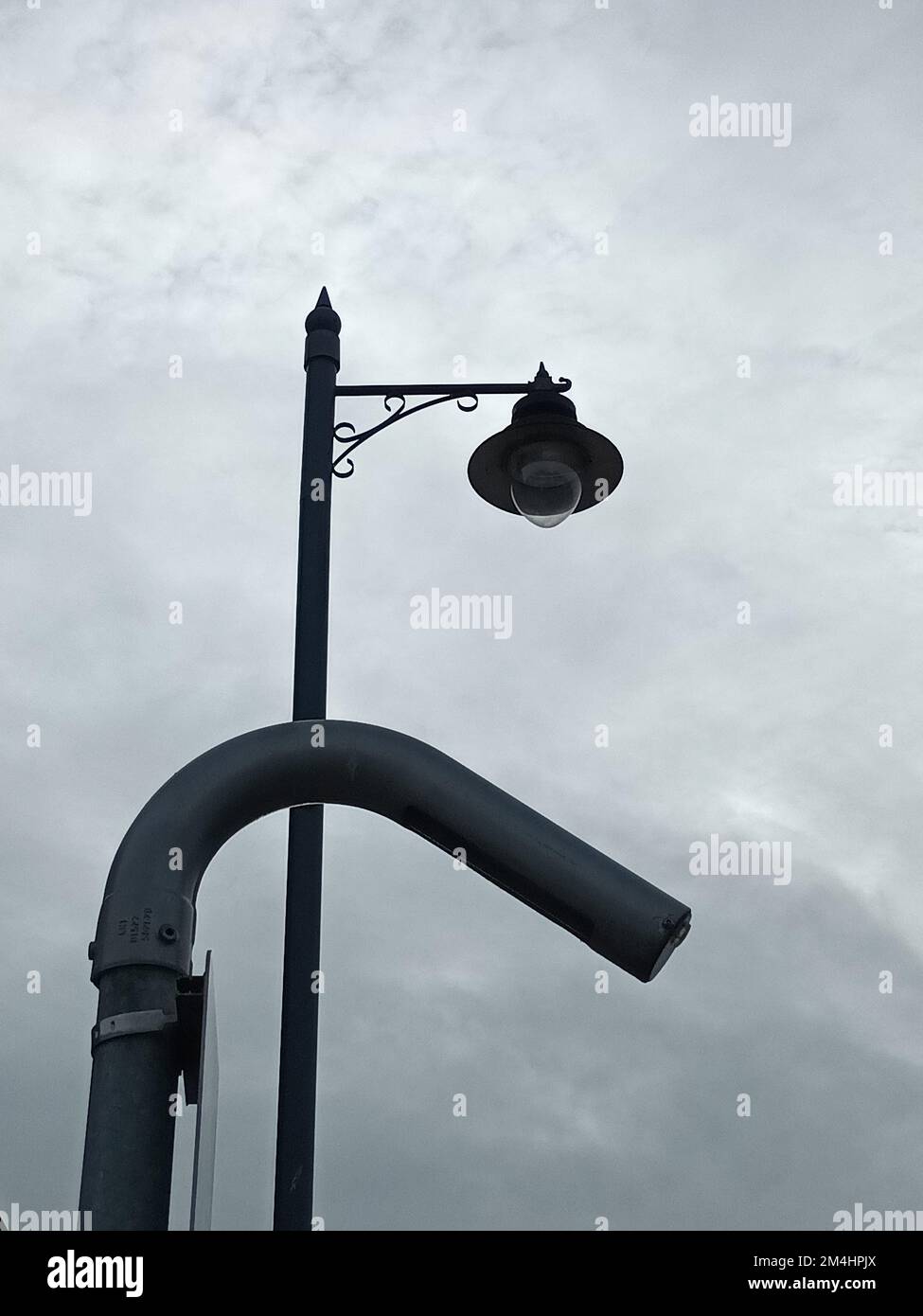 A vertical shot of a street lamp on the road in daylight in cloudy sky ...