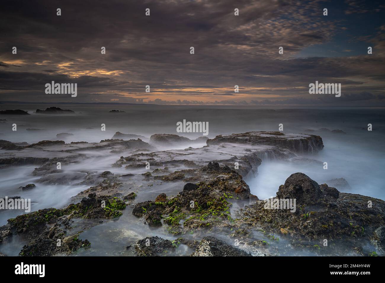 A breathtaking view of Karang Bokor Sawarna in Indonesia under dark cloudy sunset sky, long ...