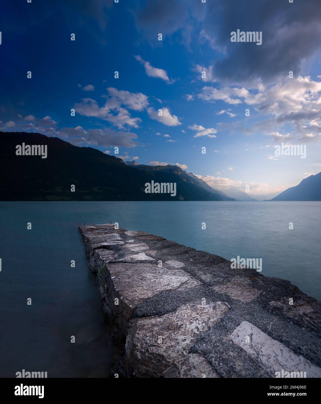 A vertical shot of a jetty on a lake overlooking mountains under a ...