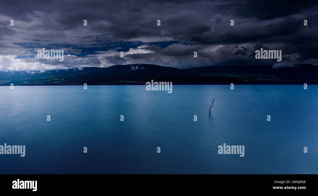 A scenic shot of the calm waters of a lake underneath a cloudy sky ...