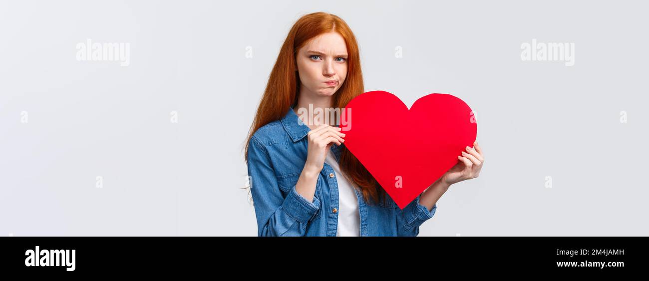 Serious-looking troubled, unsure cute redhead girl thinking what gift ...