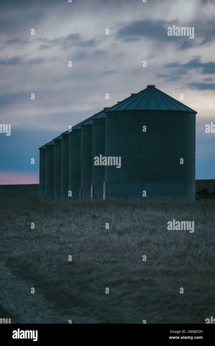 A vertical shot of several lined up steel silos during a scenic sunset ...