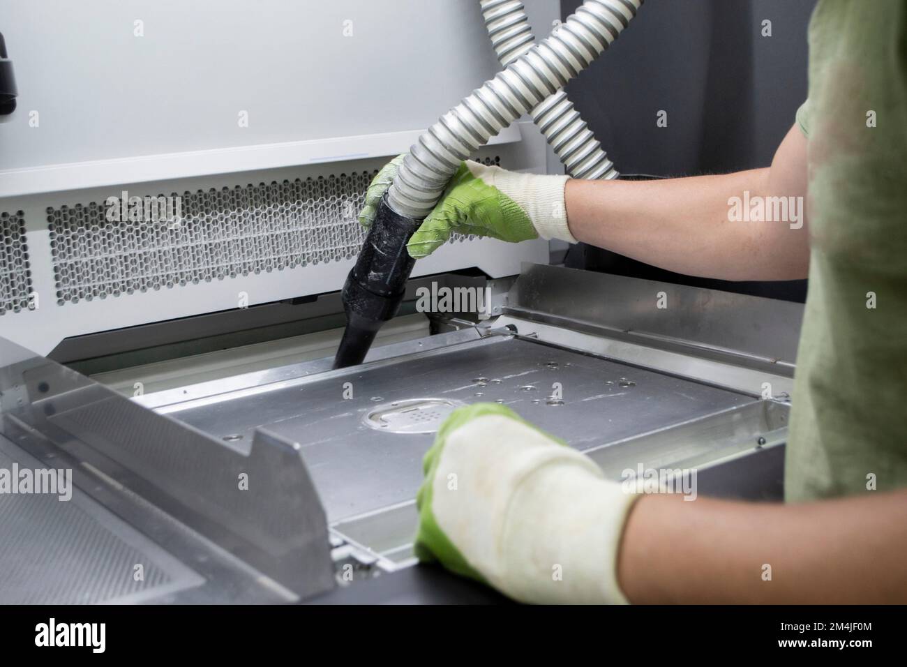 A male worker cleans the surface of an industrial 3D printer from white ...