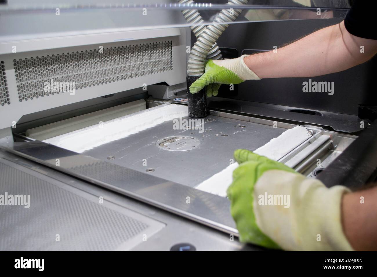 A male worker cleans the surface of an industrial 3D printer from white ...