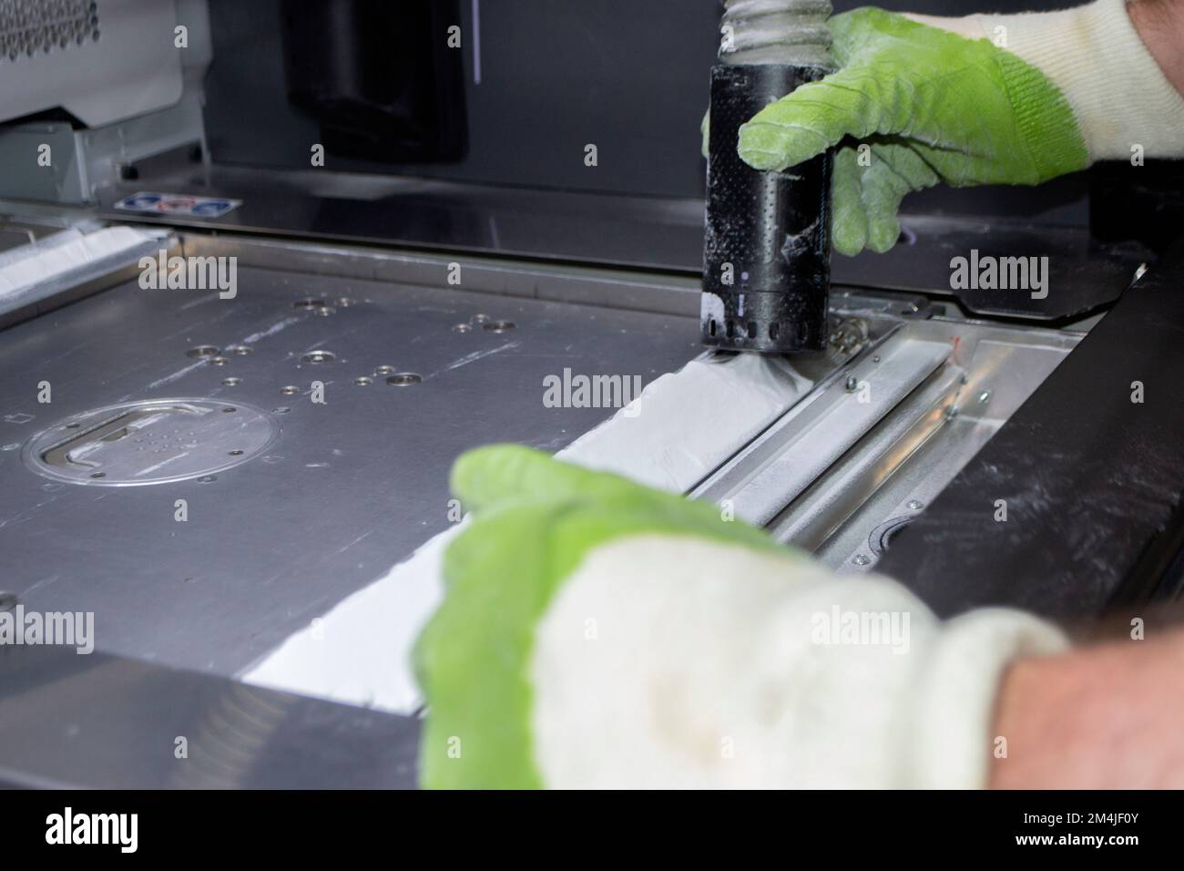 A male worker cleans the surface of an industrial 3D printer from white ...