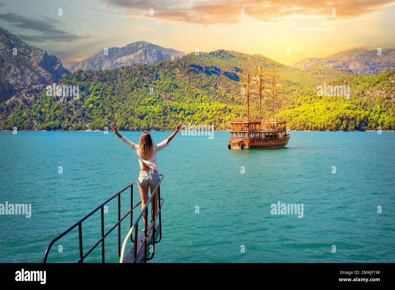 Girl with outstretched hands on bow of boat floating on azure water on ...